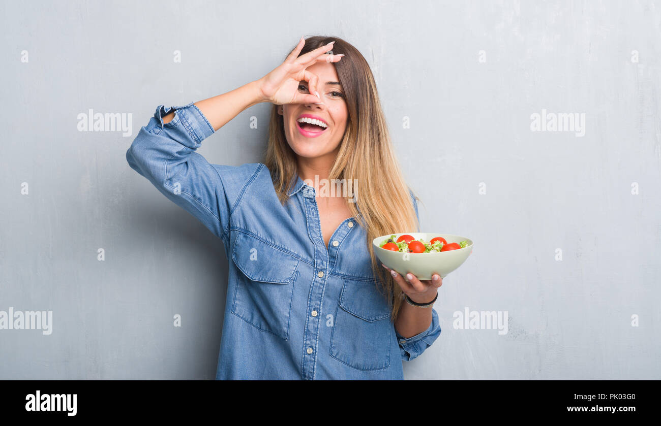 Young adult woman over grey grunge wall eating healthy tomato salad ...