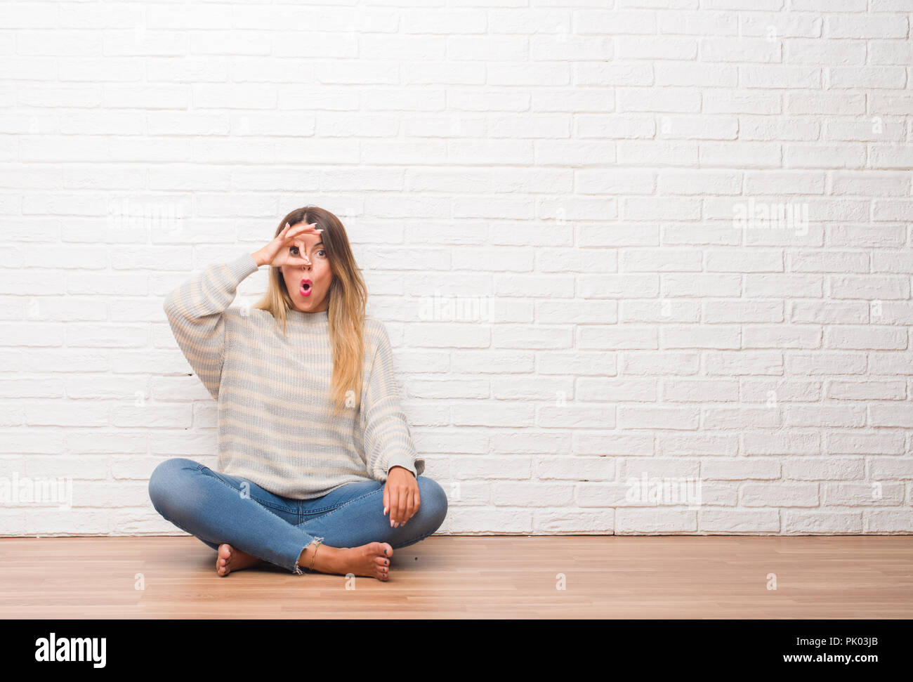 Young adult woman sitting on the floor over white brick wall at home ...