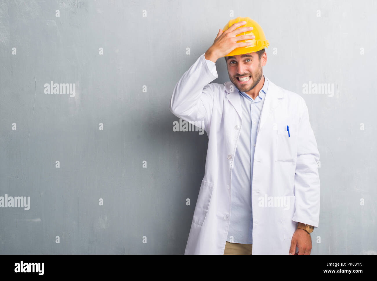 Handsome young engineer man over grey grunge wall wearing safety helmet ...