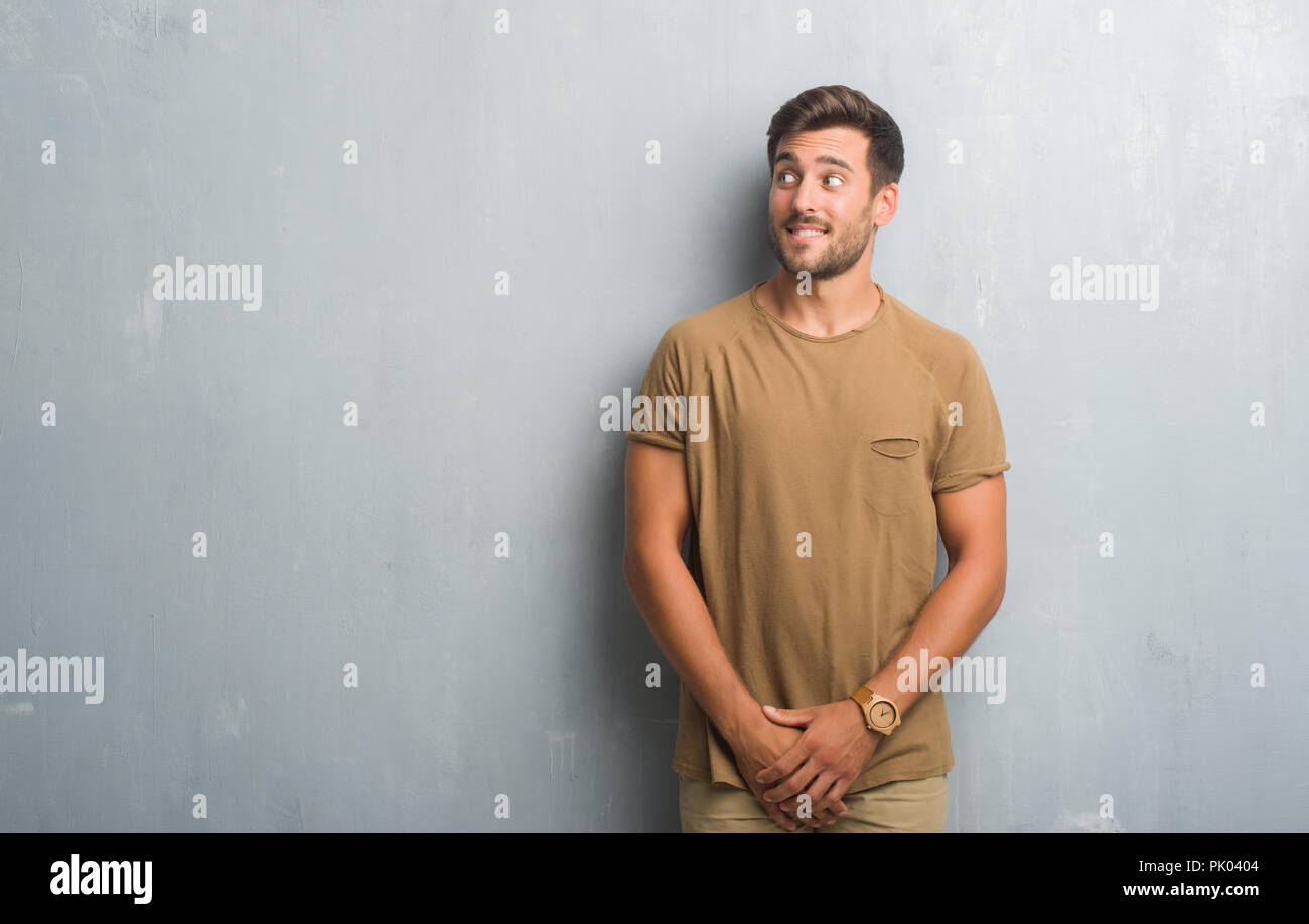 Handsome young man over grey grunge wall smiling looking side and ...
