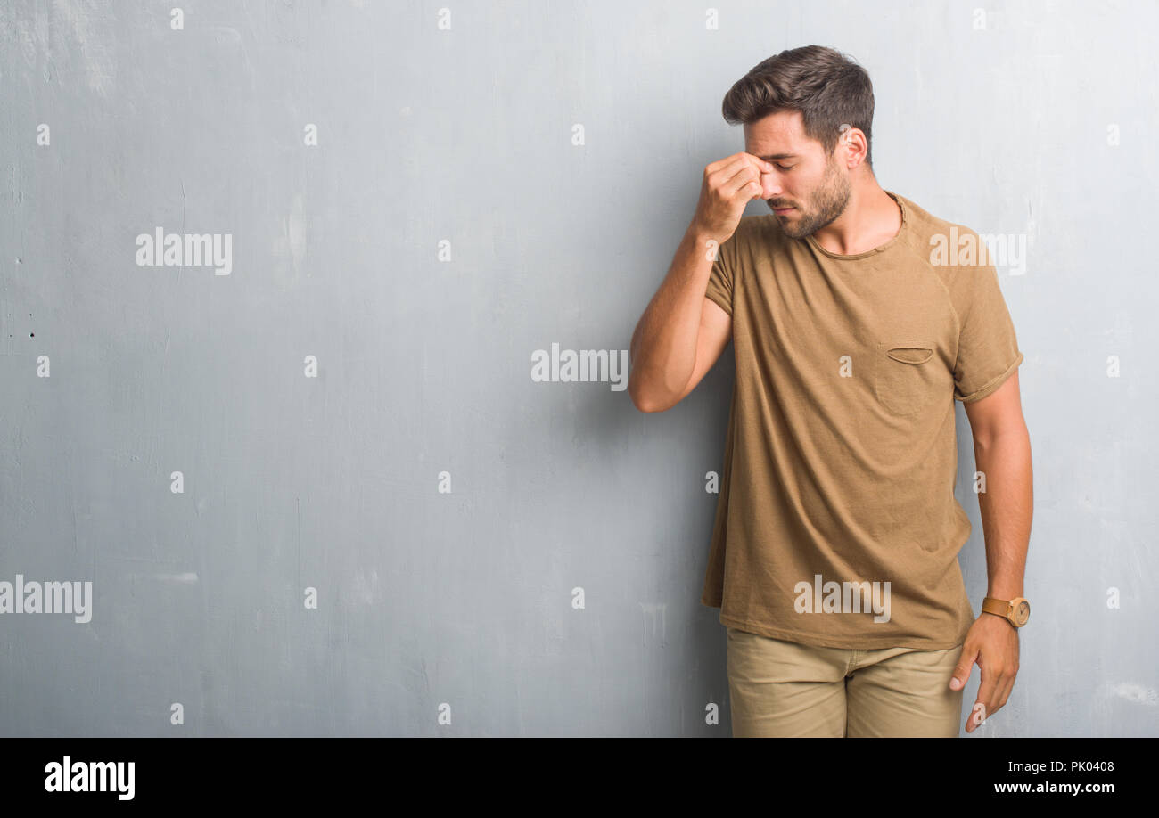 Handsome young man over grey grunge wall tired rubbing nose and eyes ...