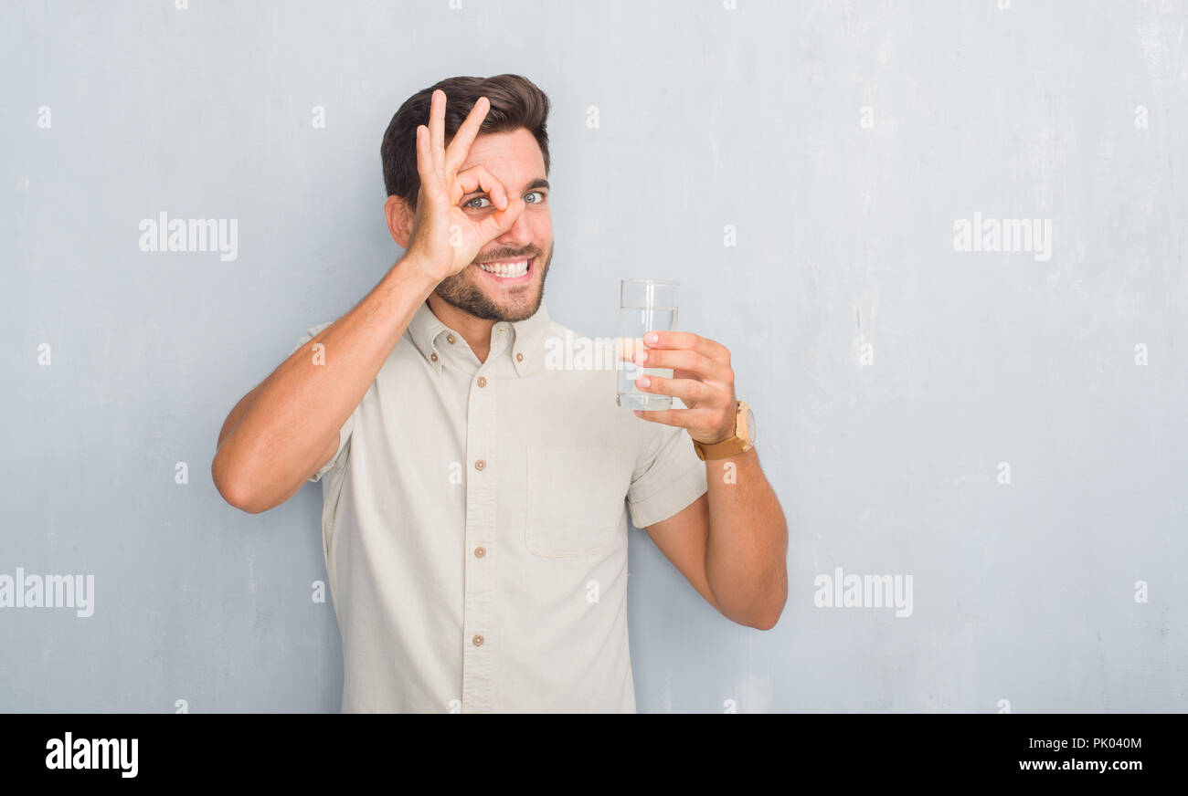 Handsome young man over grey grunge wall drinking glass of water with ...
