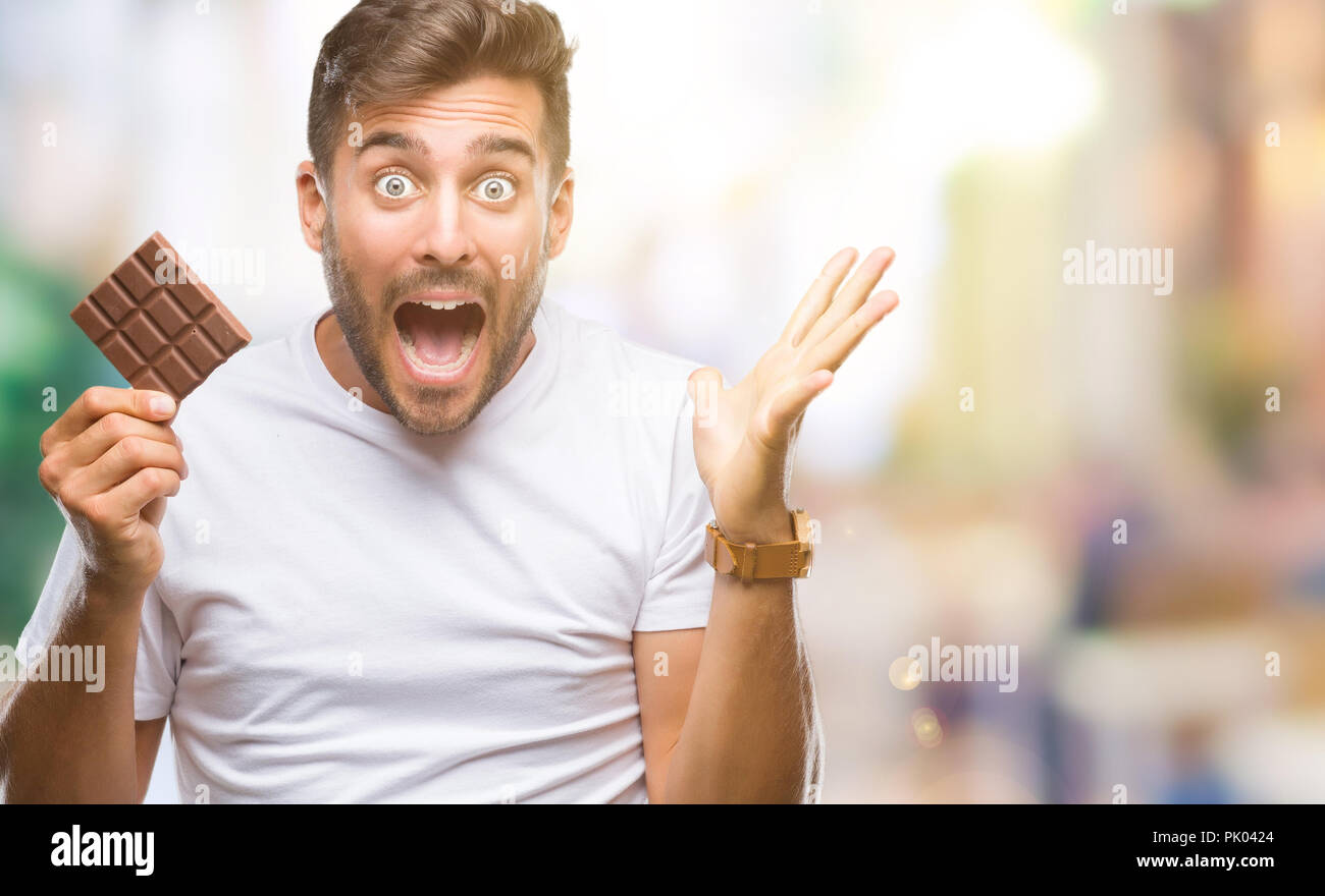 Young handsome man eating chocolate bar over isolated background very ...