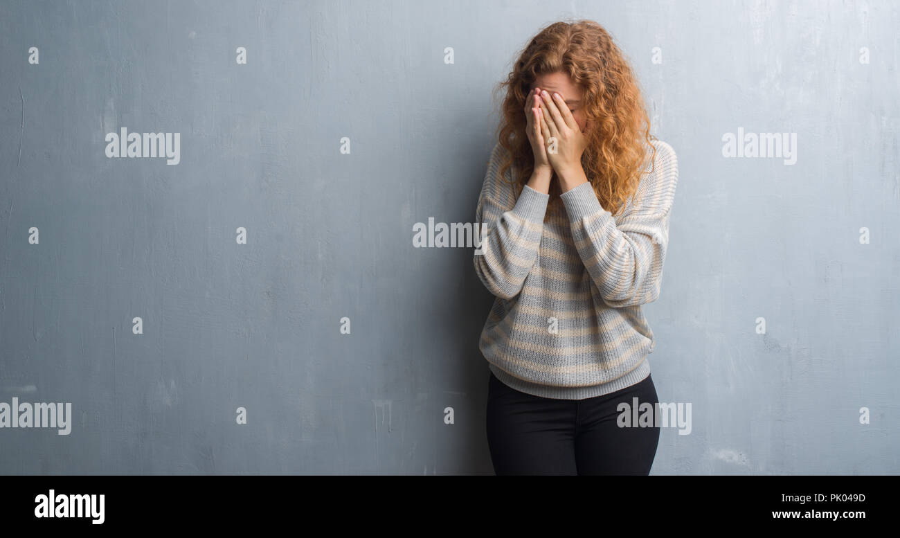 Young redhead woman over grey grunge wall with sad expression covering ...