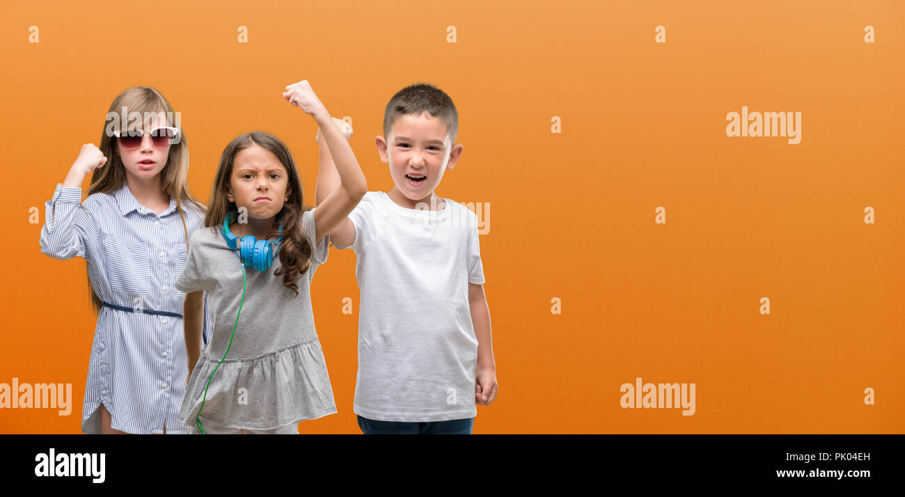 Group of boy and girls kids over orange background annoyed and ...