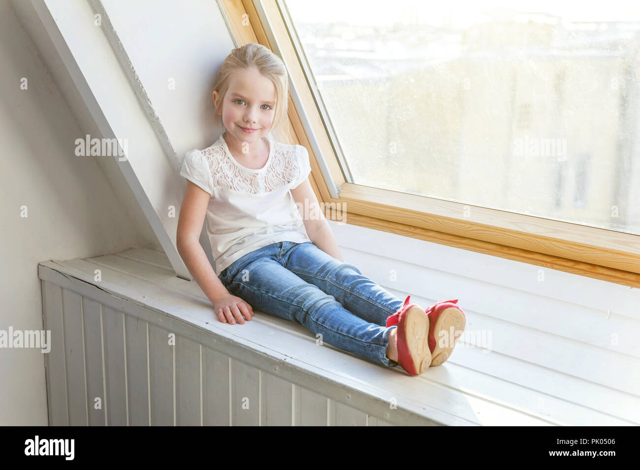 Little cute sweet smiling girl in jeans and white T-shirt sitting on ...