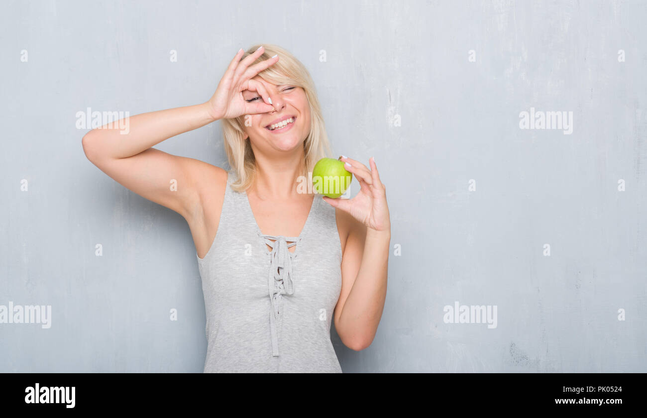Adult caucasian woman over grunge grey wall eating green apple with ...