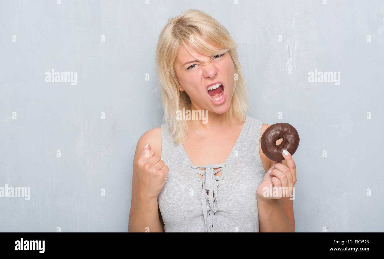 Caucasian adult woman over grey grunge wall eating chocolate donut ...