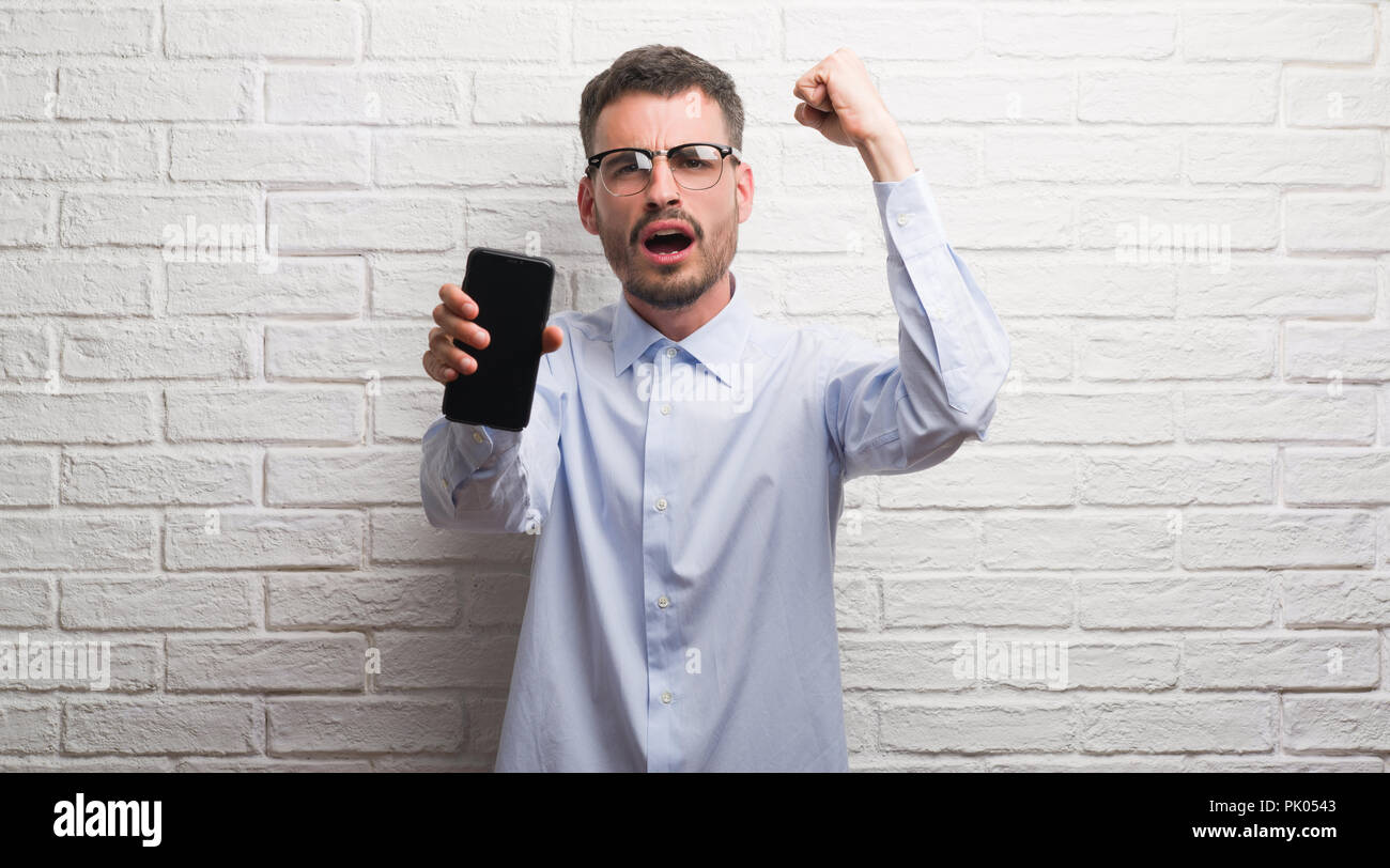Young adult man talking on the phone standing over white brick wall ...