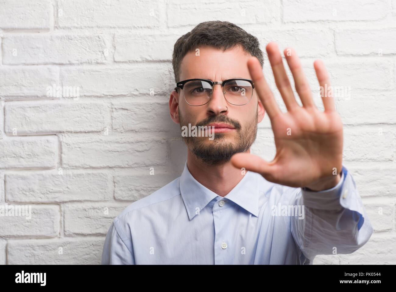 Young adult business man standing over white brick wall with open hand ...