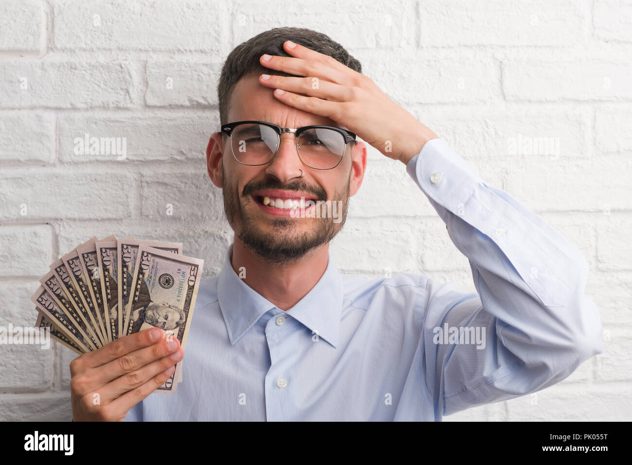 Young hipster business man holding dollars stressed with hand on head ...