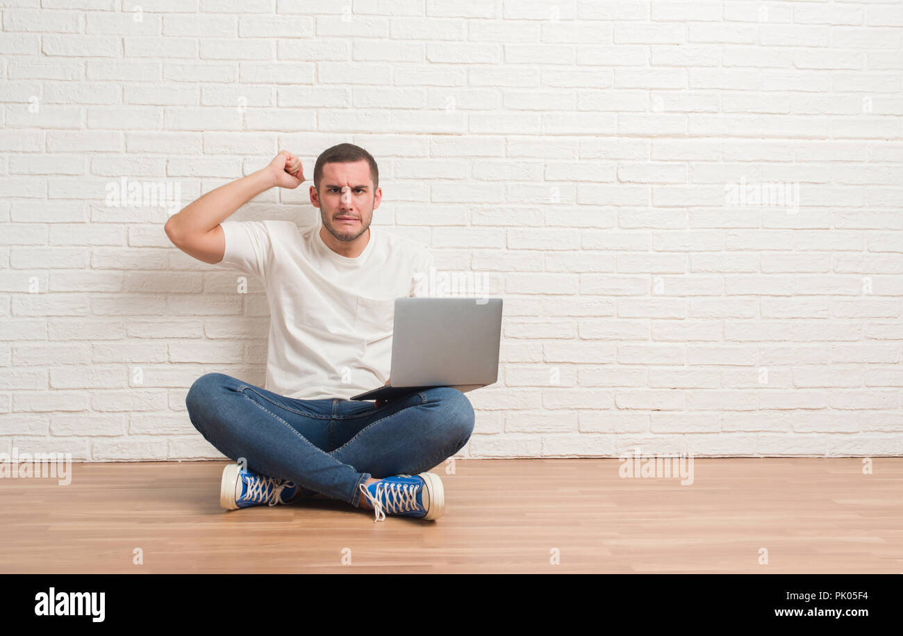 Young caucasian man sitting over white brick wall using computer laptop ...