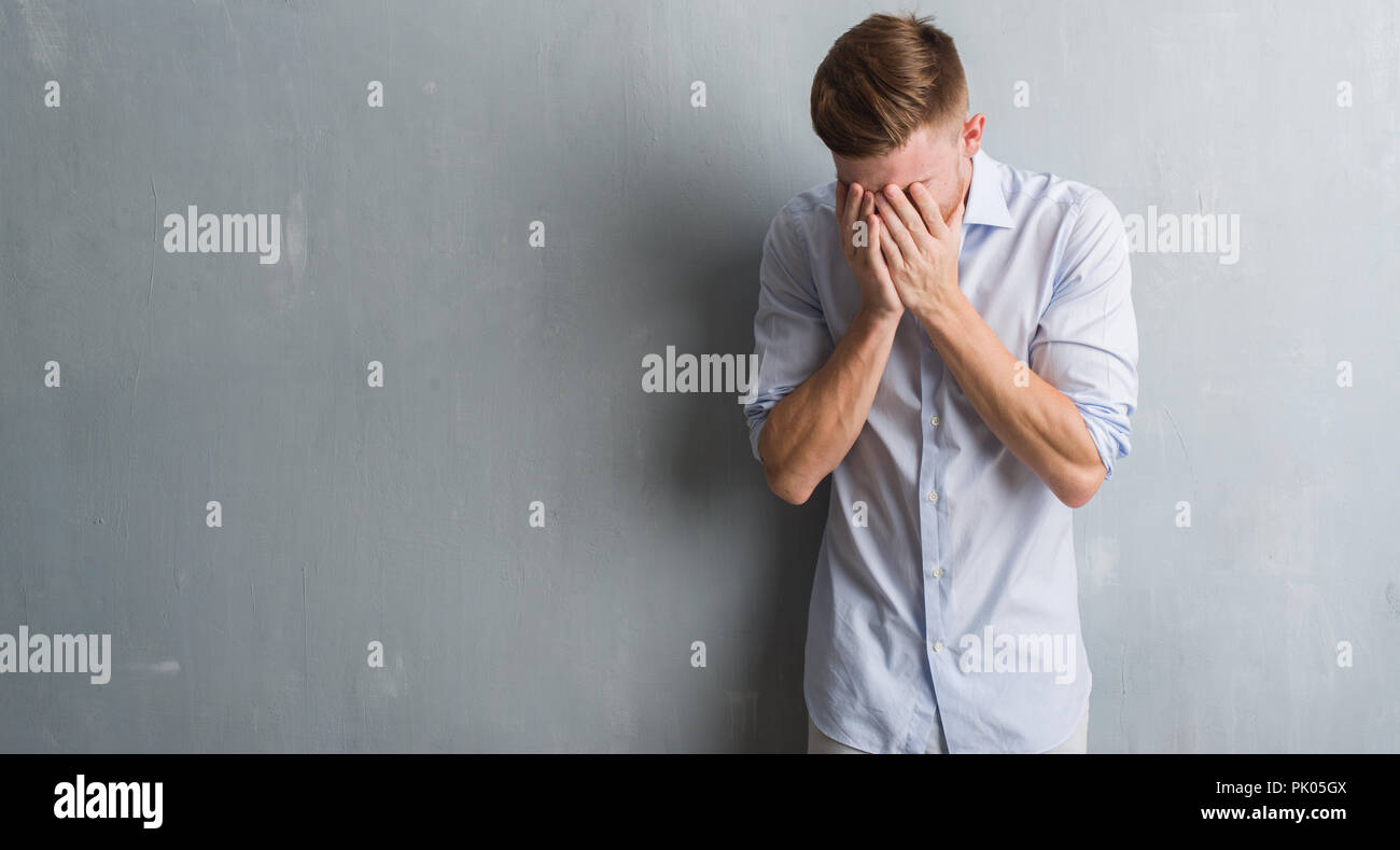 Young redhead business man over grey grunge wall with sad expression ...
