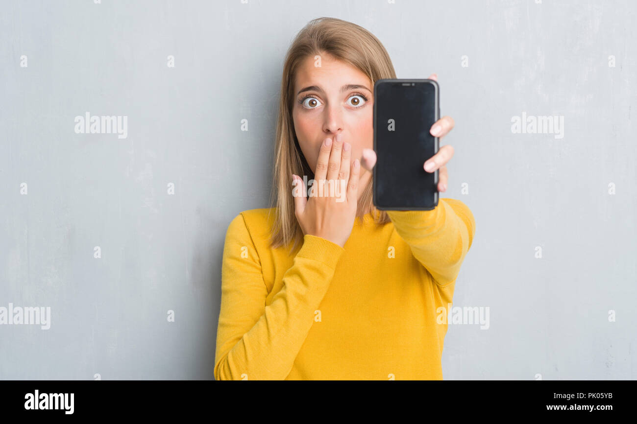 Beautiful young woman over grunge grey wall showing smartphone screen ...