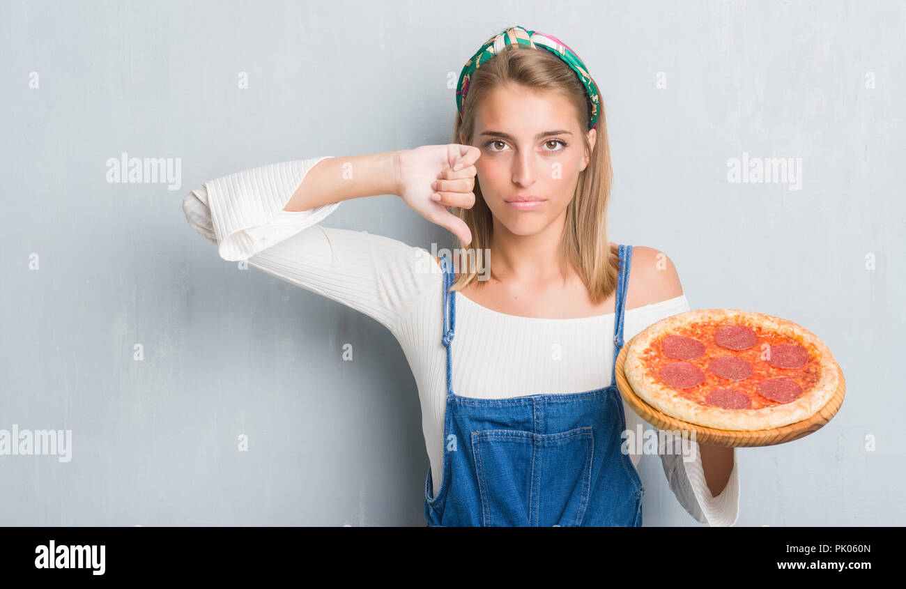 Beautiful young woman over grunge grey wall eating pepperoni pizza with ...