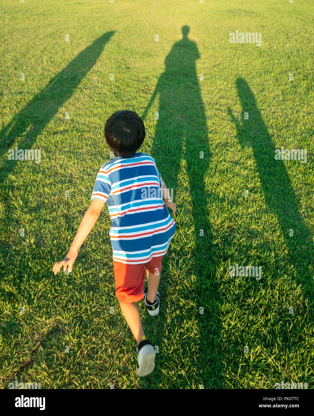 An Asian boy watching and running toward family's shadows on the grass ...