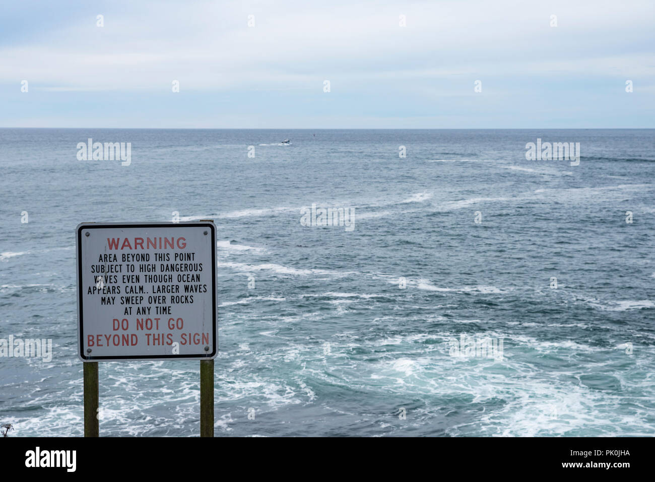 Warning sign on the beach at Depot Bay advises of high, dangerous waves ...