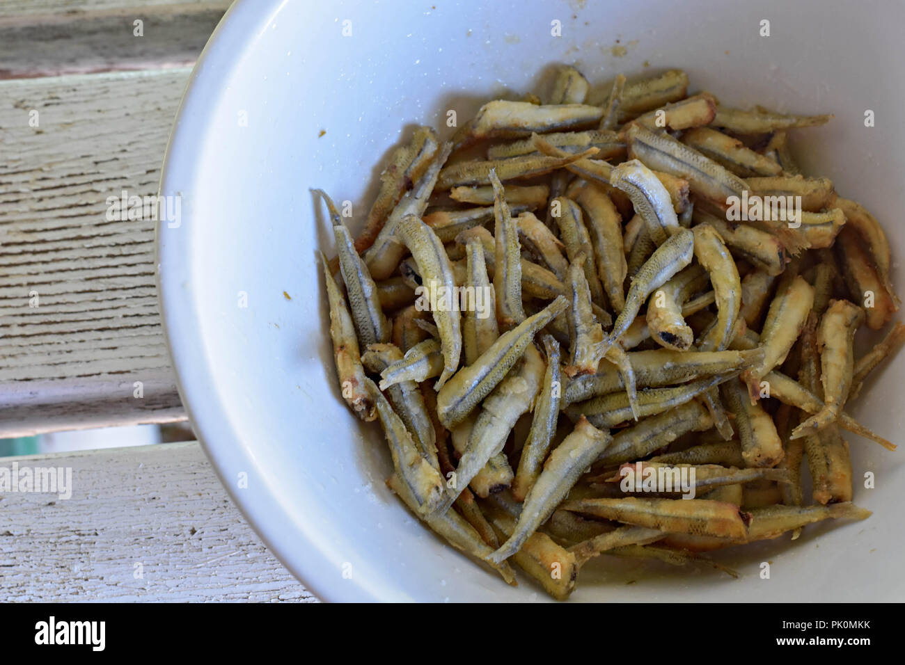 Small crunchy fried sea fish in the white bowl at wooden table as ...