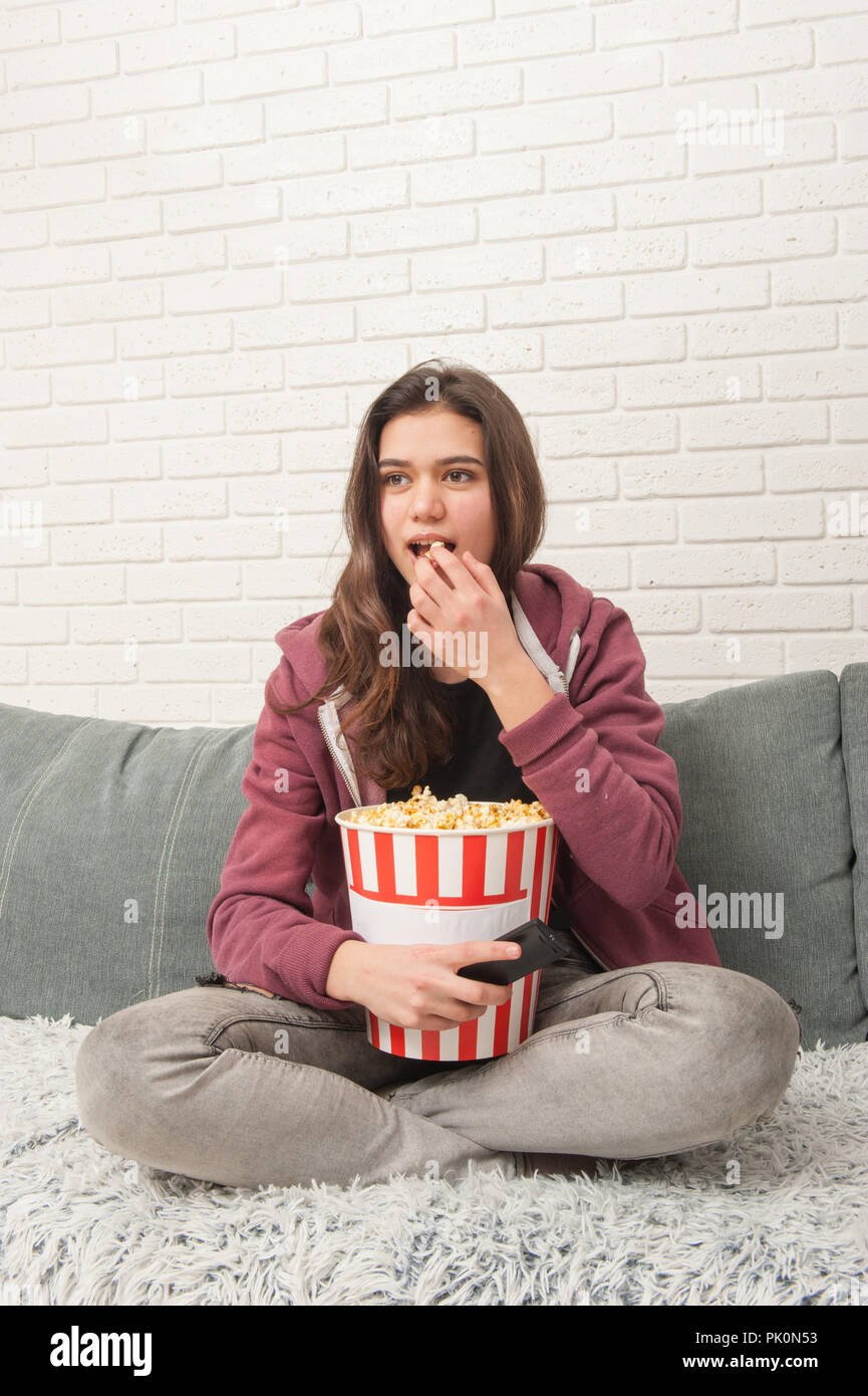 A teenage girl is sitting on the couch and eating popcorn Stock Photo ...