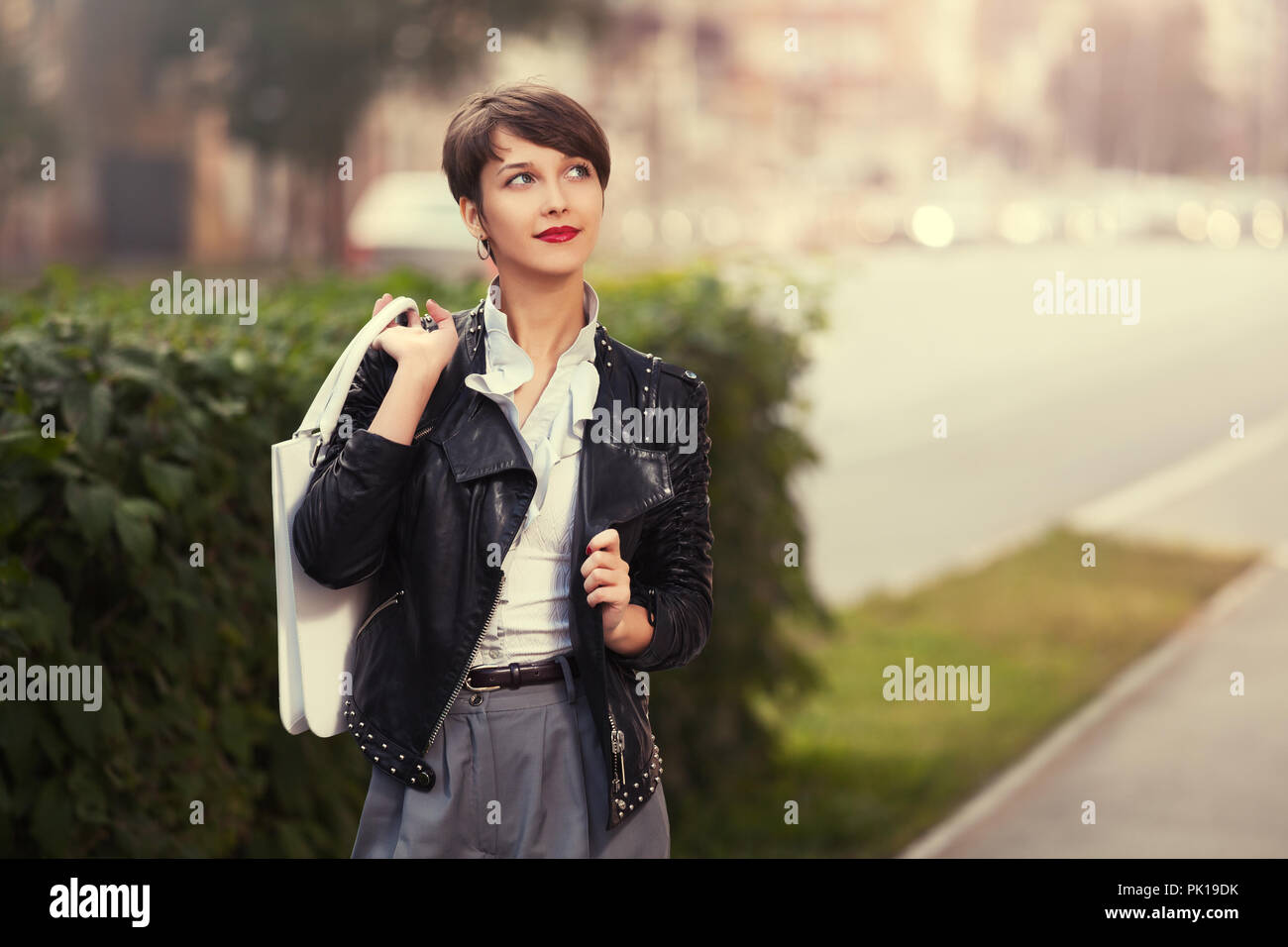 Happy young woman with handbag walking in city street. Stylish fashion ...