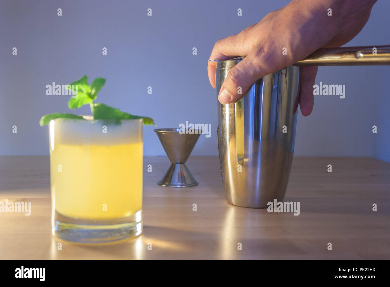 Closeup of a bartender's hand holding a cocktail shaker with a jigger and frothy drink garnished ...