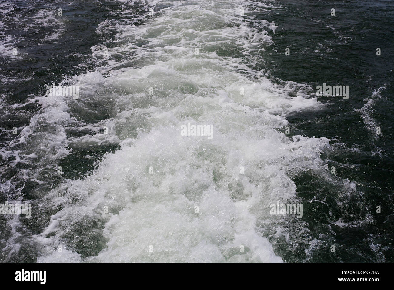 White foam on water from floating boat. Deep blue sea with trail on ...