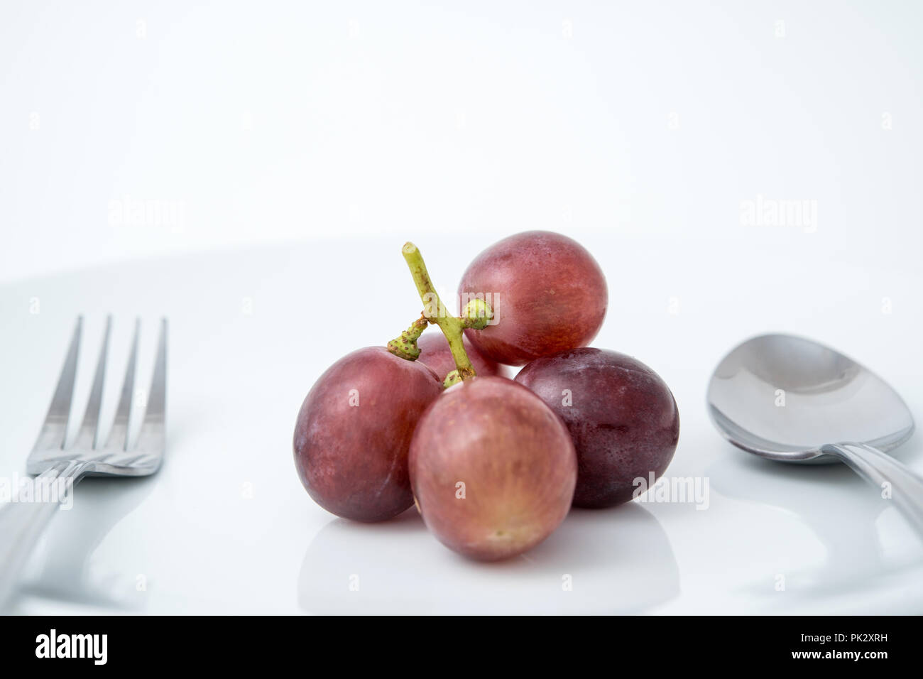 health eating of fruit, red grape on white plate with fork and spoon ...
