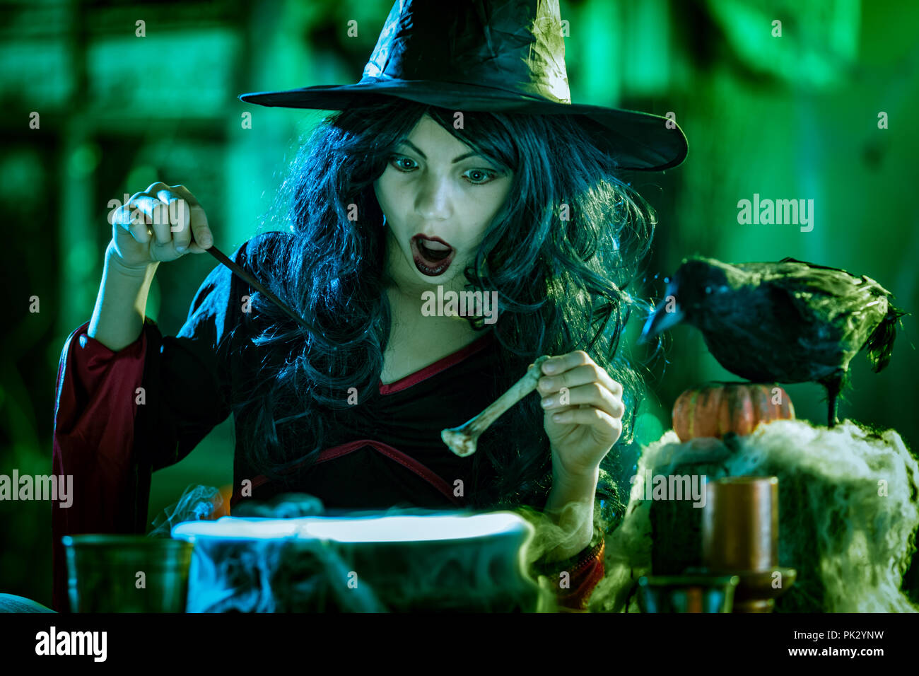 Young angry witch with awfully face tells evil words, and putting bones ...