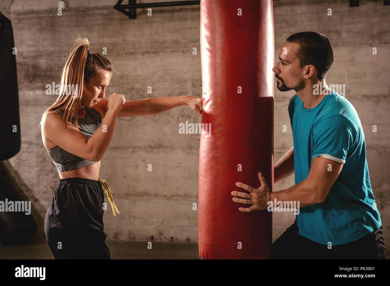 Young muscular woman punching a boxing bag on cross fit training with a ...