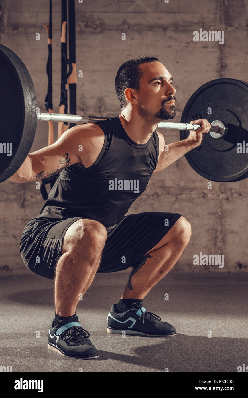 Handsome young muscular man doing squat exercise with barbell at the ...