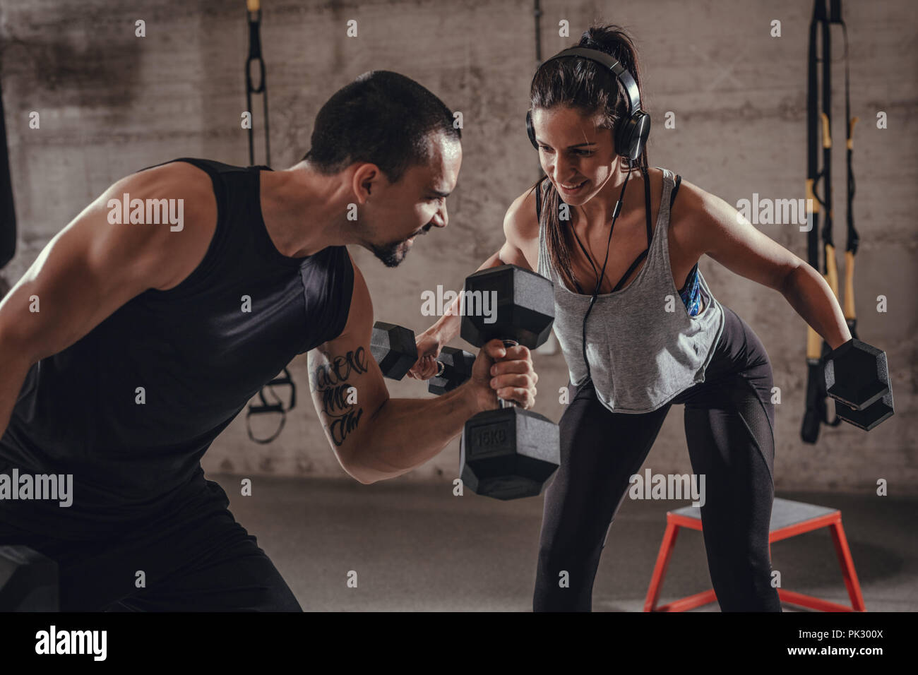 Young muscular couple doing hard exercise with dumbbells for shoulders ...