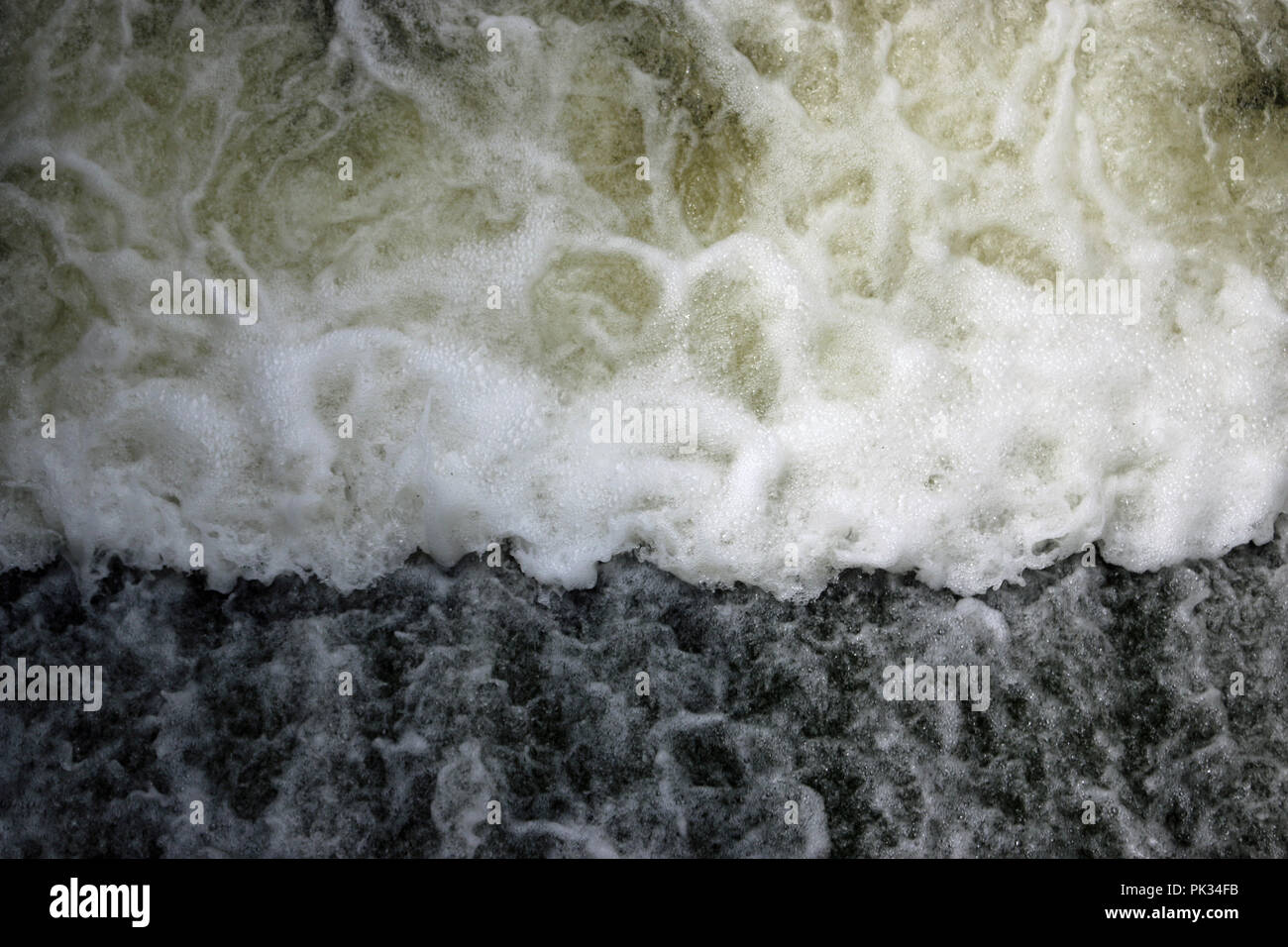 Looking down from above at water flowing over a small weir on a river ...