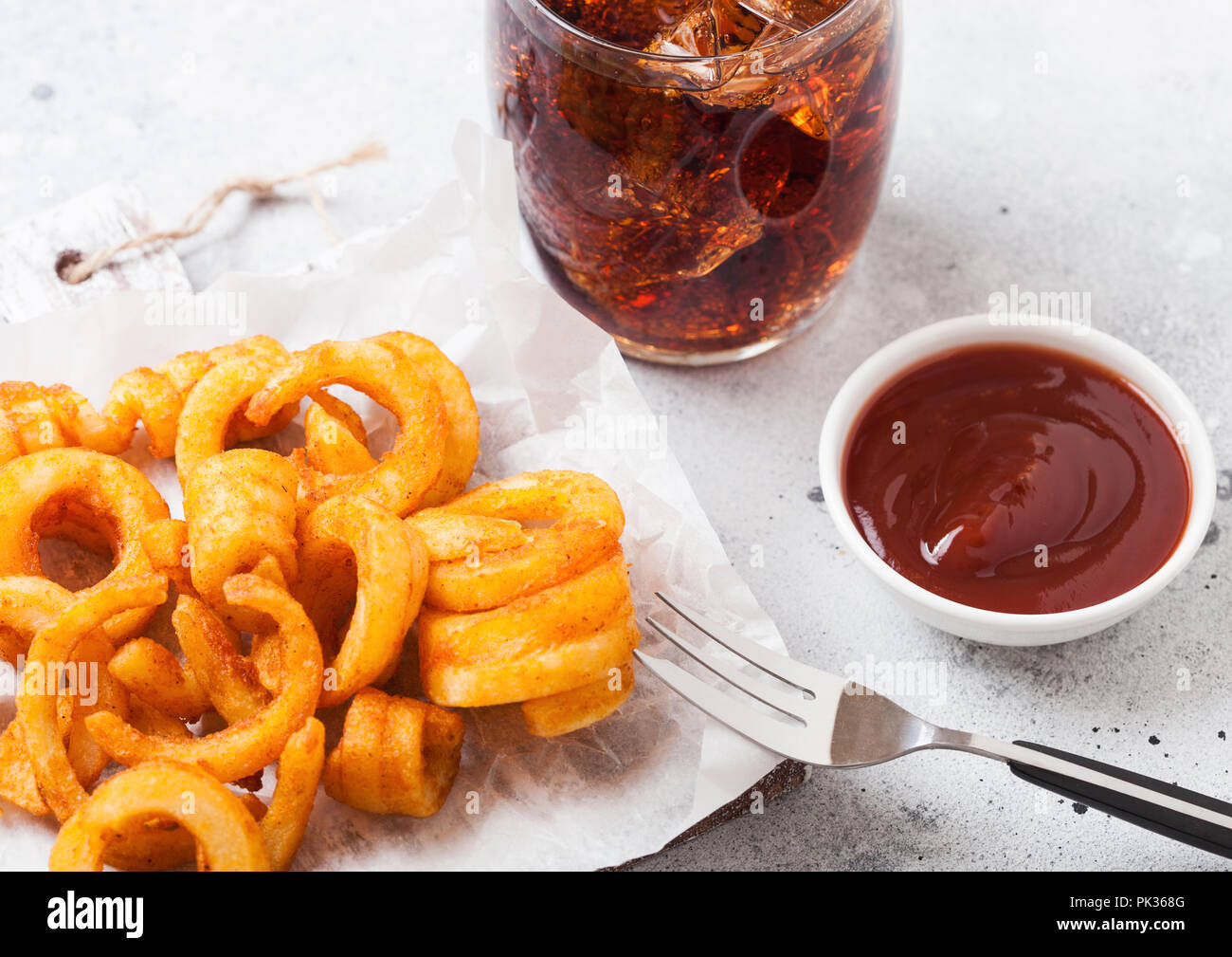 Curly fries fast food snack on wooden board with ketchup and glass of ...