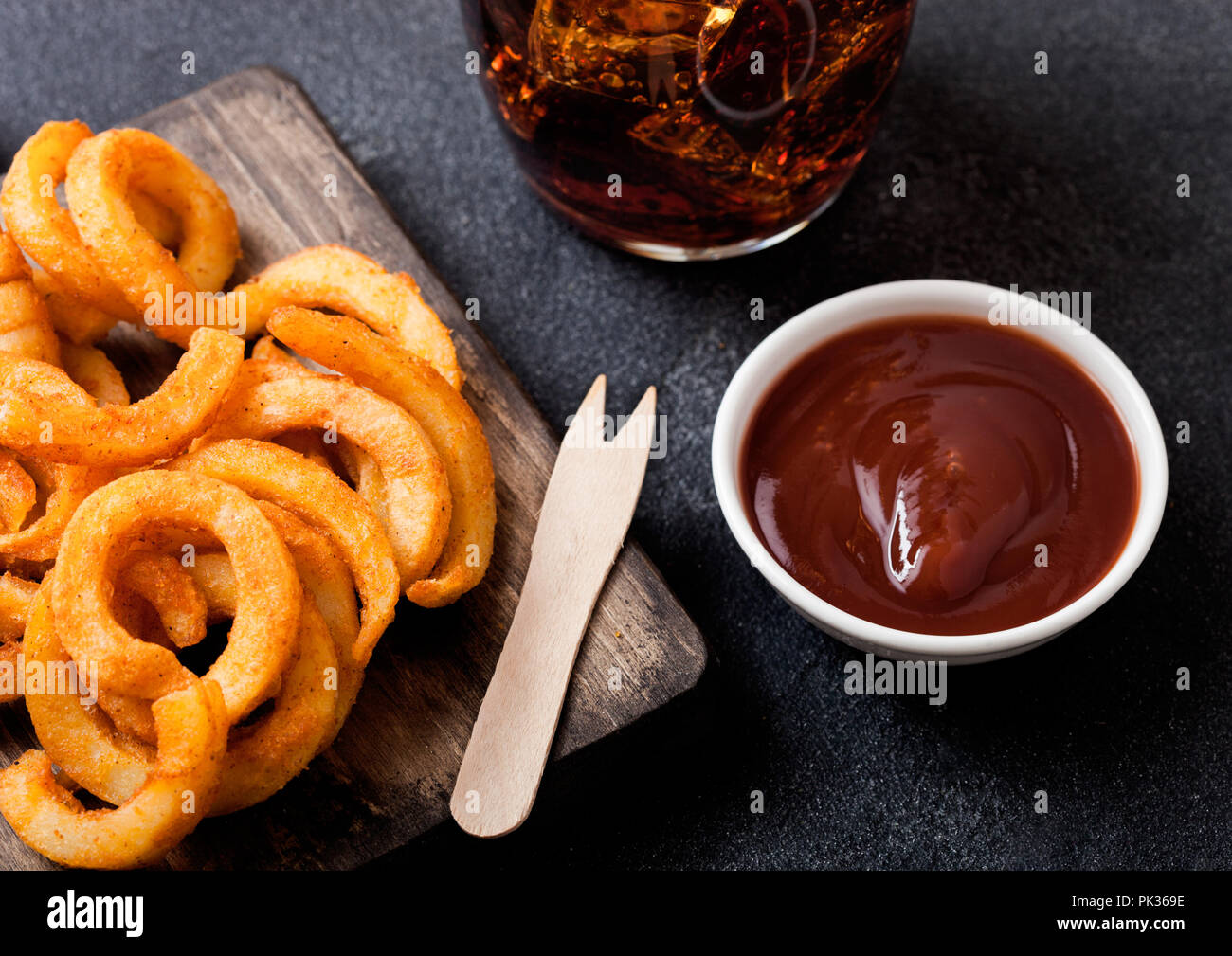Curly fries fast food snack on wooden board with ketchup and glass of ...