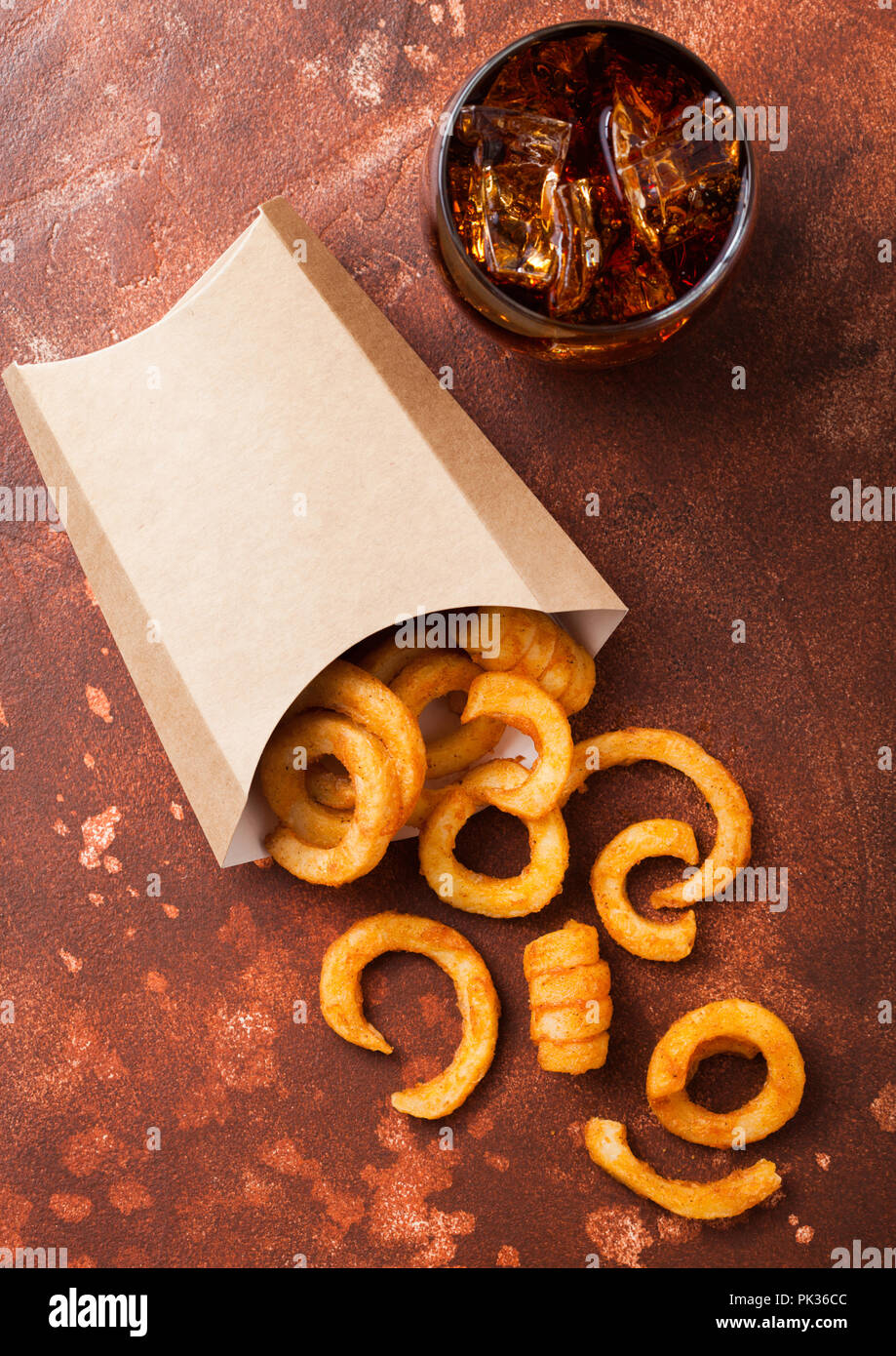 Curly fries fast food snack in paper container with glass of cola on ...