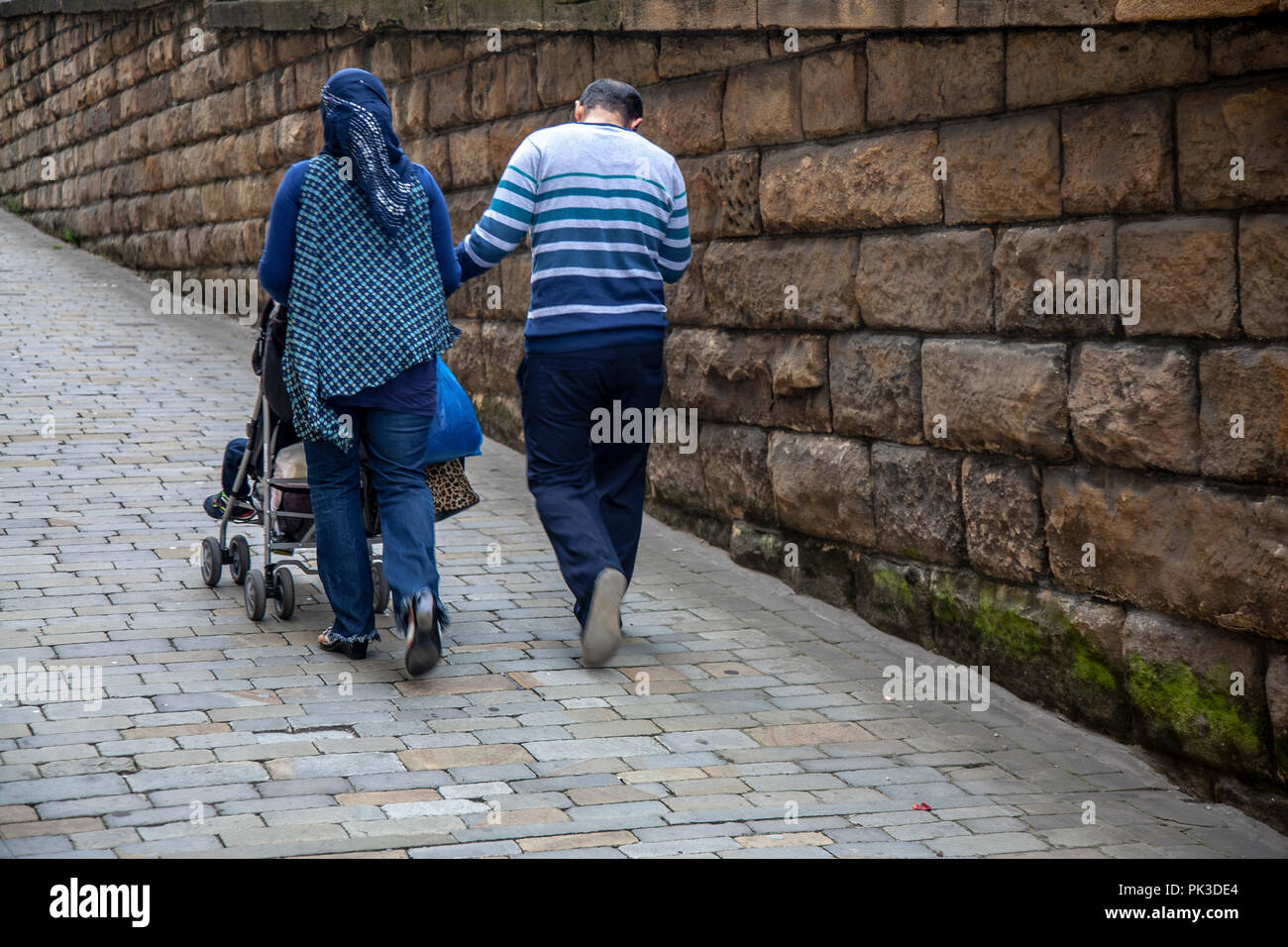 Couple pushing pram and walking away from camera up a steep hill in ...