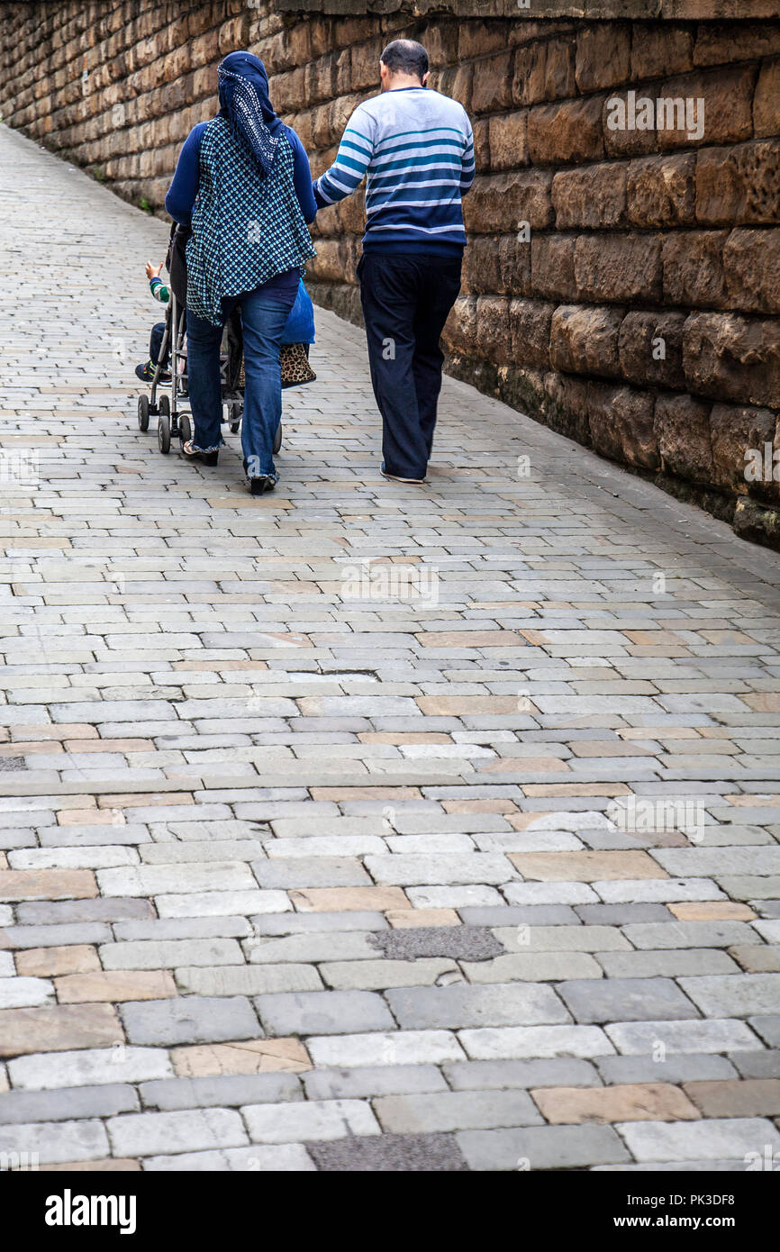 Couple pushing pram and walking away from camera up a steep hill in ...