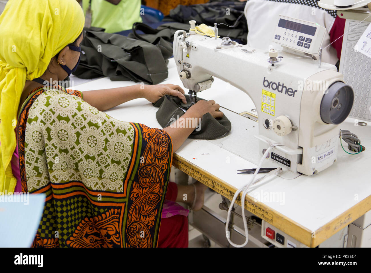 A garment worker at work on a sewing machine inside a garment factory ...