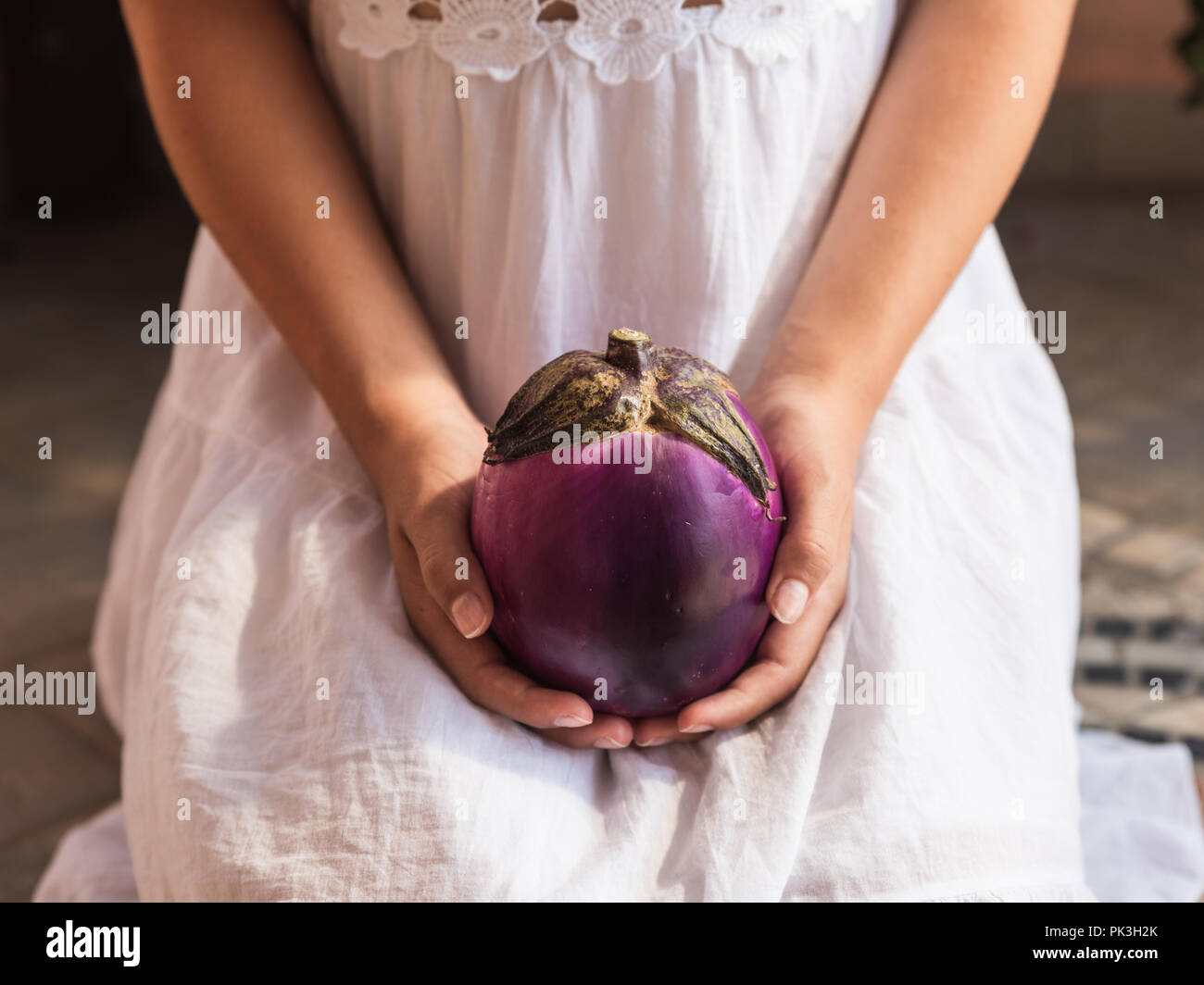 Girl dressed in white holds, holding a big purple, pink courgette ...