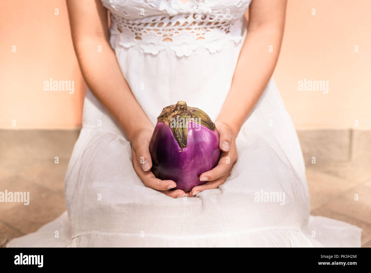 Girl dressed in white holds, holding a big purple, pink courgette ...