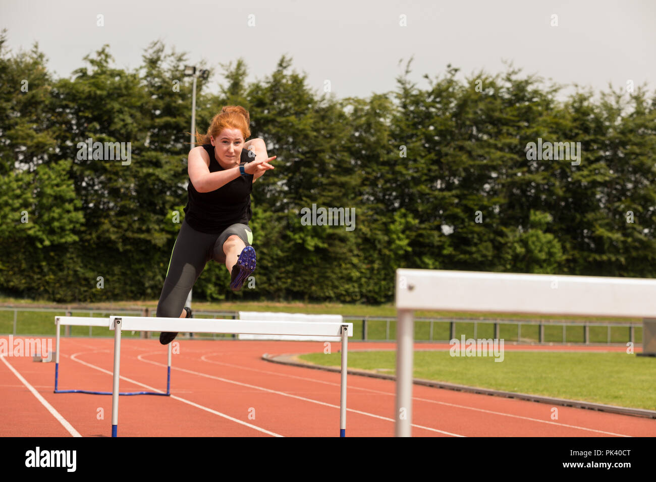 Female athletic jumping over hurdle on sports track Stock Photo - Alamy