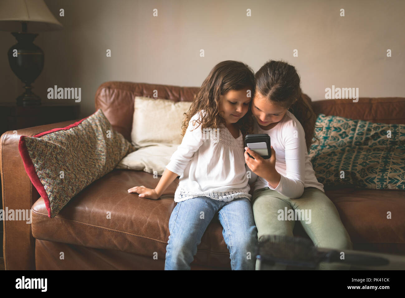 Girls using mobile phone on sofa Stock Photo - Alamy