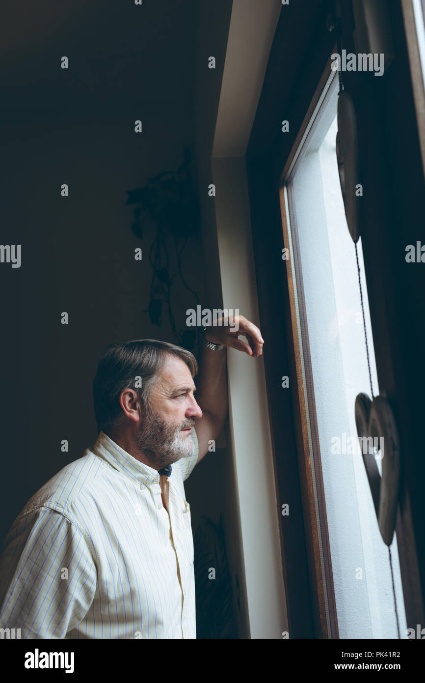 Senior man looking through window at home Stock Photo - Alamy