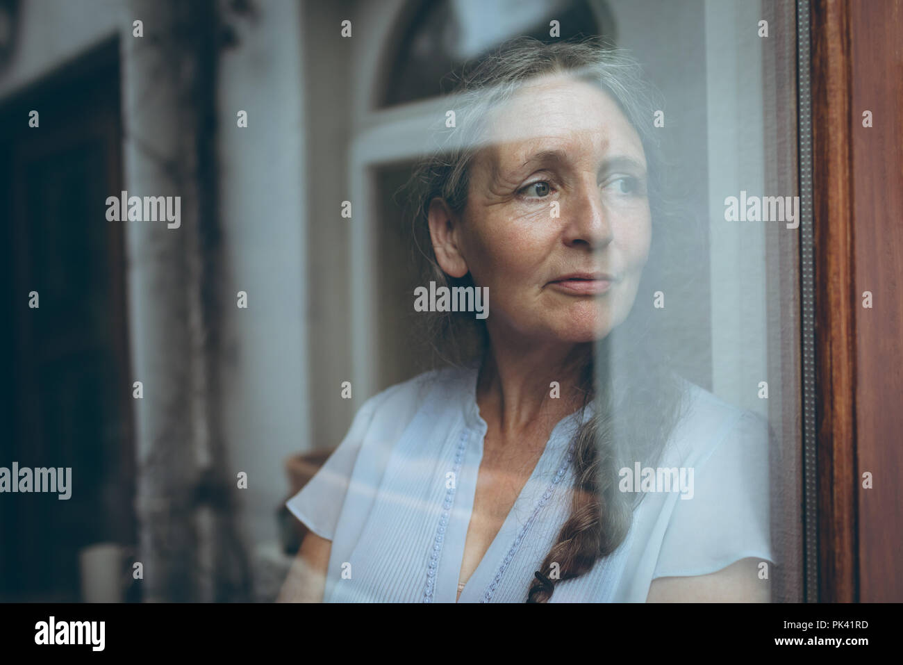 Senior woman looking through window at home Stock Photo - Alamy