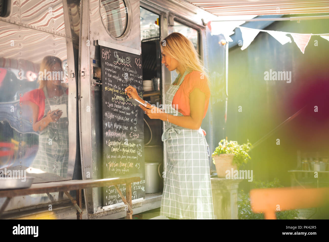 Female waitress writing menu on menu board while using digital tablet ...