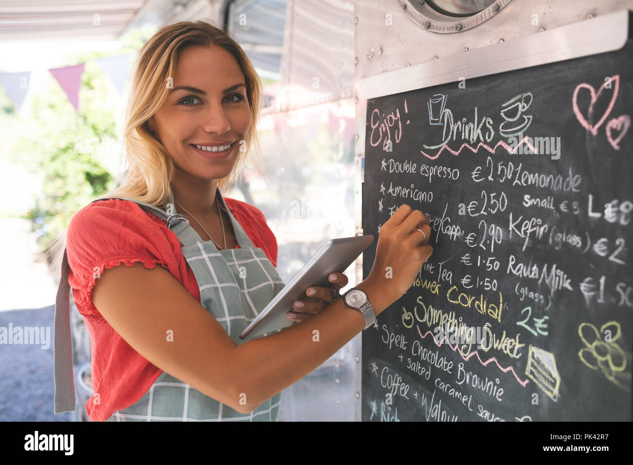 Female waitress writing menu on menu board while using digital tablet ...