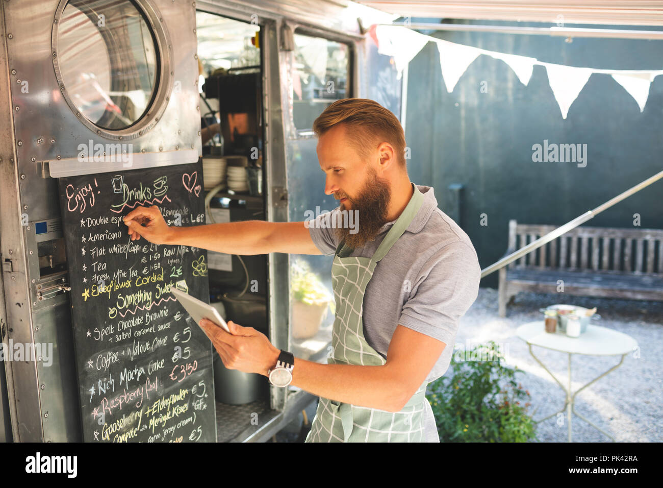 Male waitress writing menu on menu board while using digital tablet ...