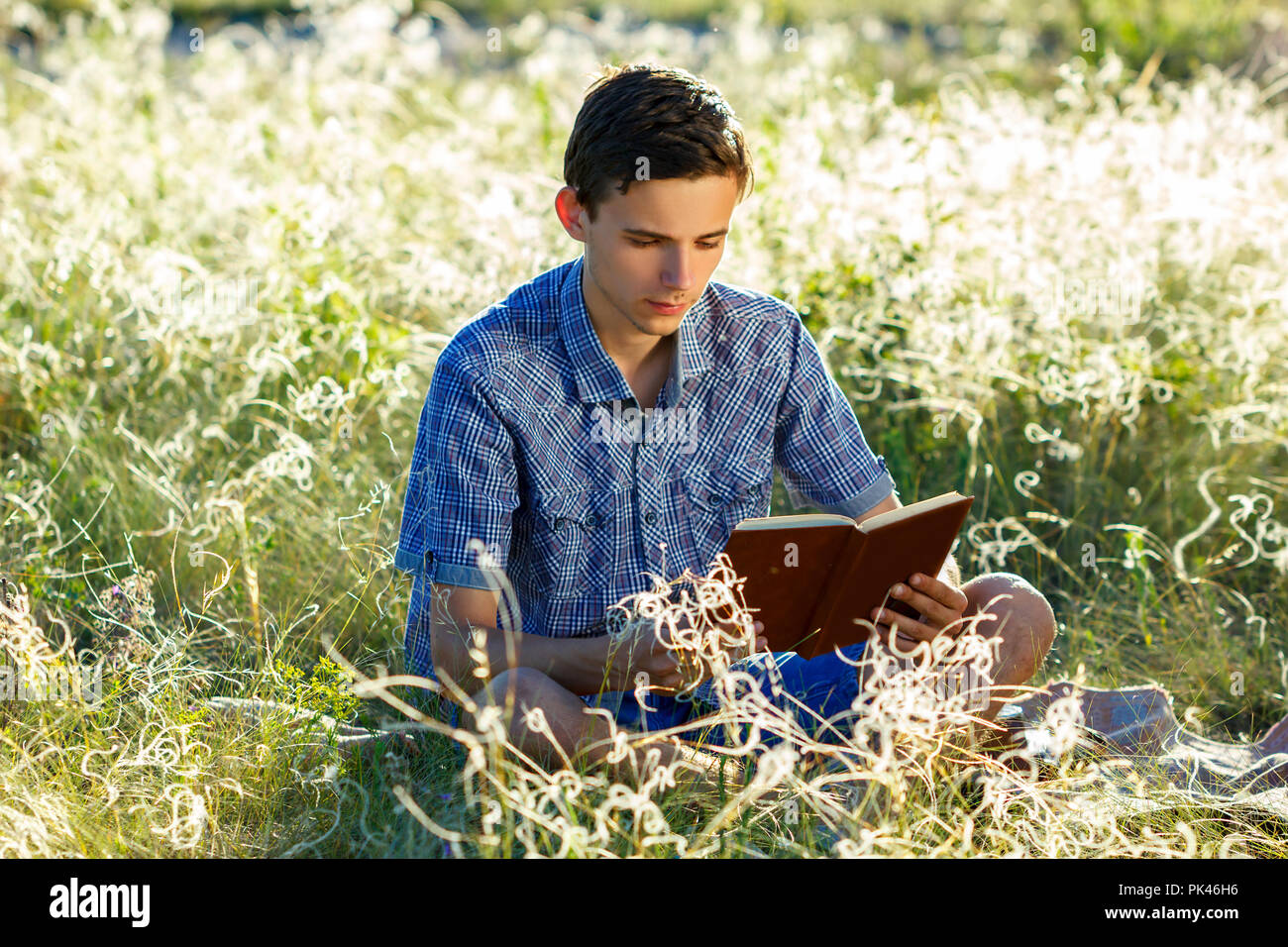 young man sitting in nature reading a book Stock Photo - Alamy