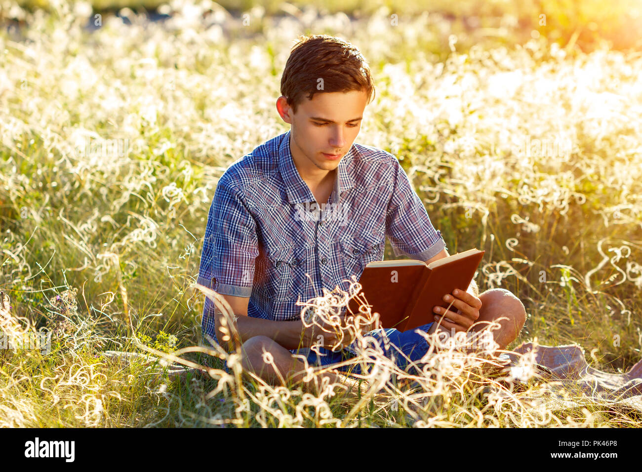young man sitting in nature reading a book Stock Photo - Alamy