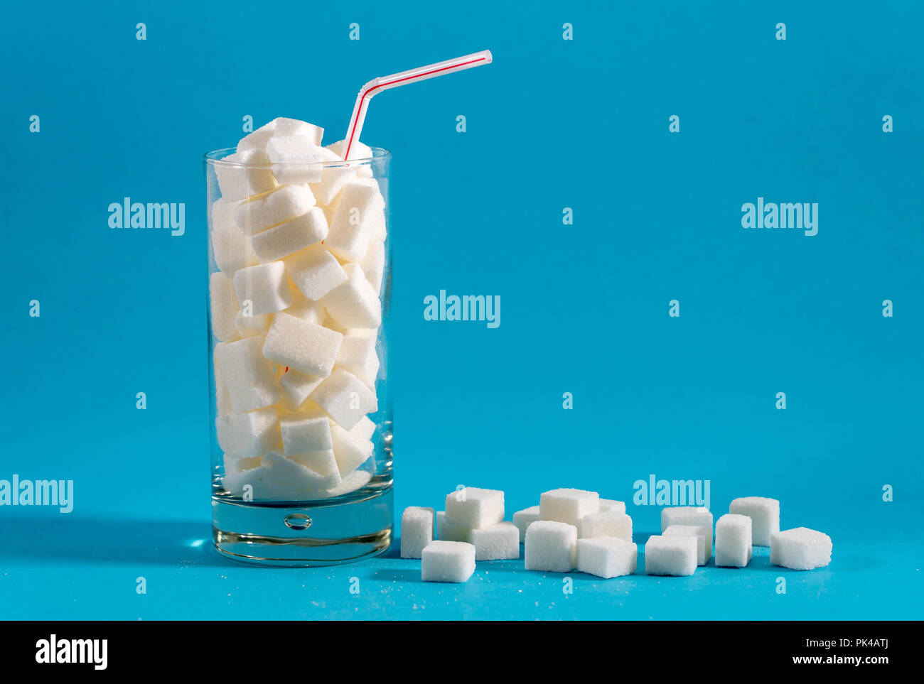 Glass with red stripes straw filled with sugar cubes on blue background ...